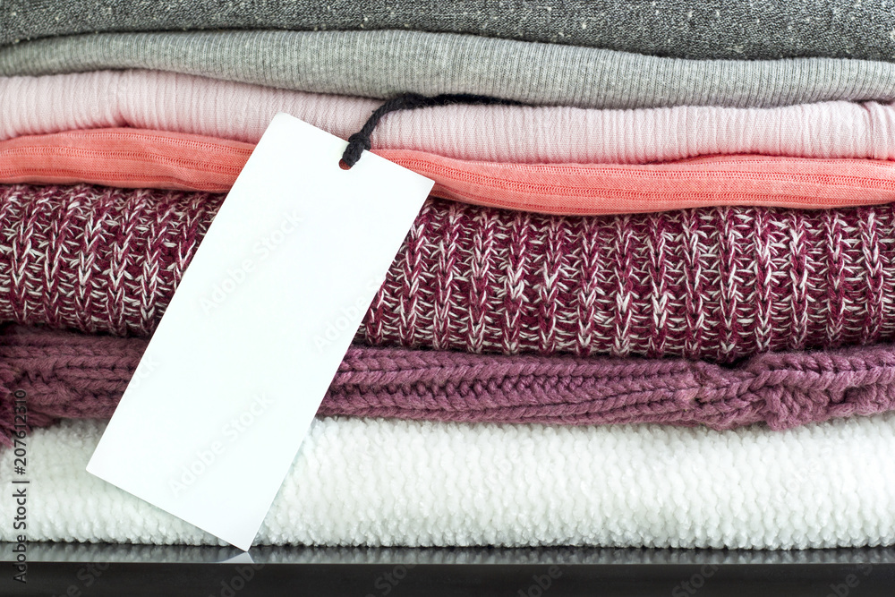 Label white price tag on stack of folded colorful clothes. Mockup label ...