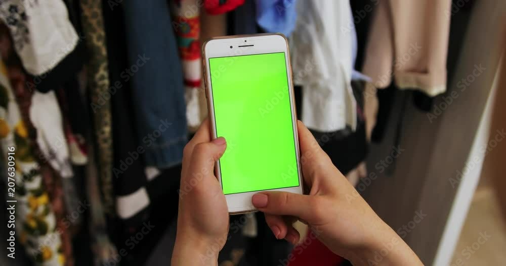 Close up woman hand holding use smart phone with vertical green screen in background of wardrobe ...