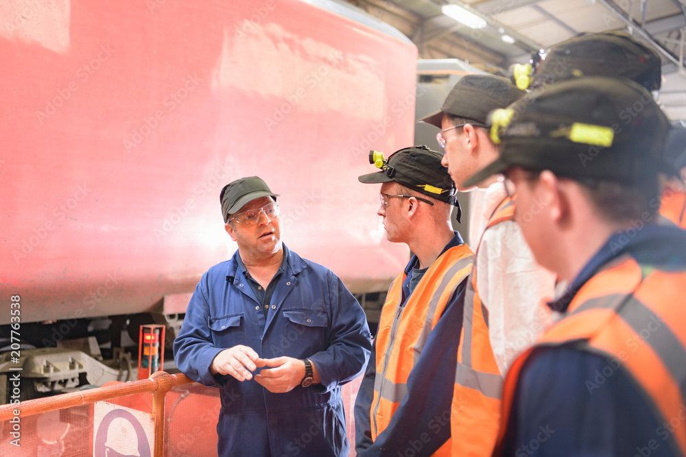 Engineer instructing apprentices with locomotive wheel lathe in train ...