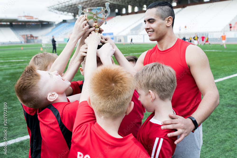 Portrait of junior football team holding trophy together and cheering ...