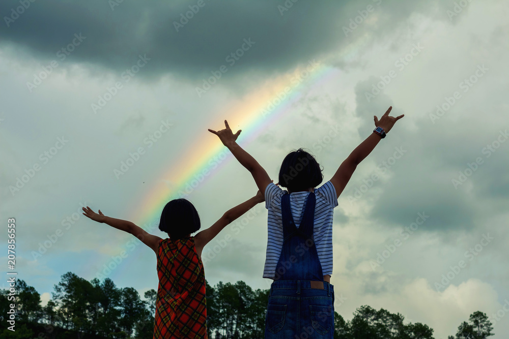 Children playing under cloudy sky with rainbow. Stock Photo | Adobe Stock