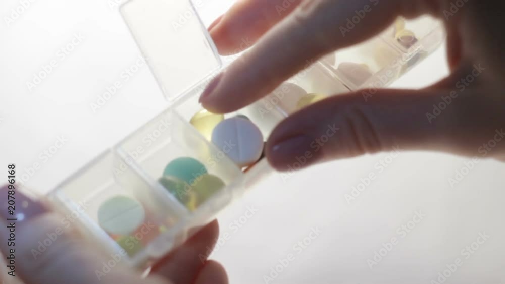 Woman opens part of the plastic box with pills and takes the largest ...