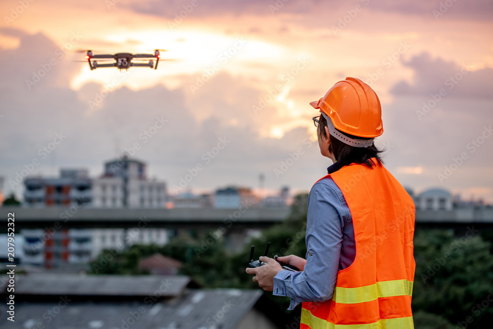 Young Asian engineer flying drone over construction site during sunset ...