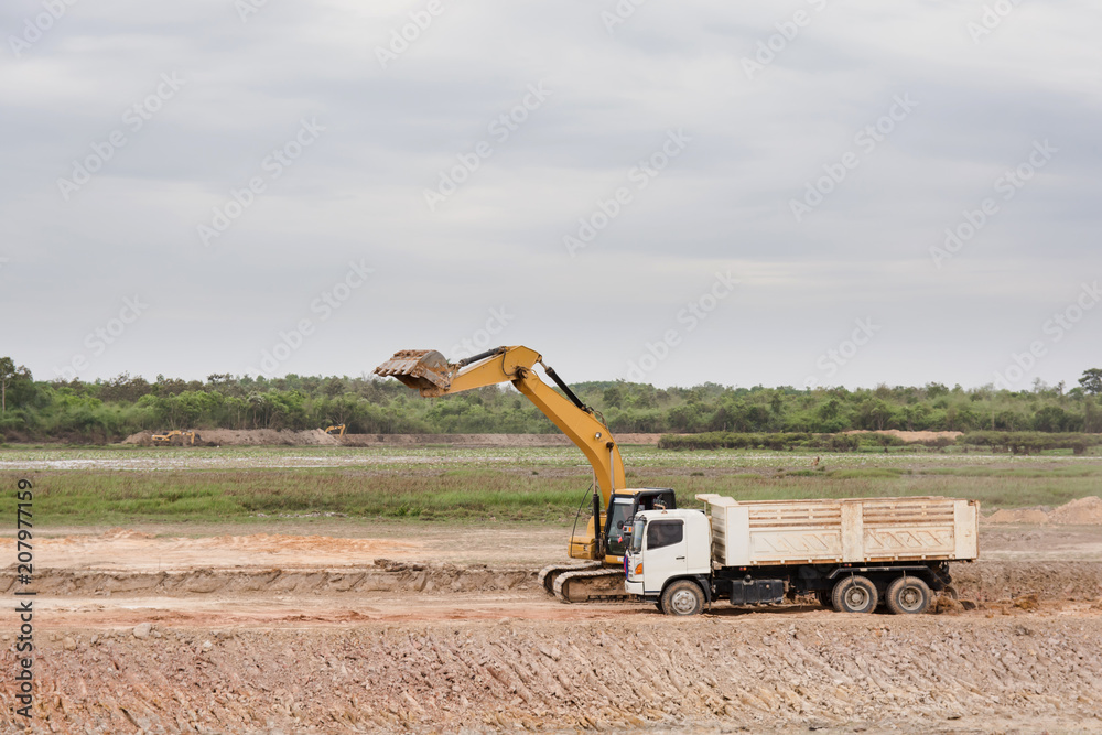 Yellow excavator machine loading soil into a dump truck at construction ...