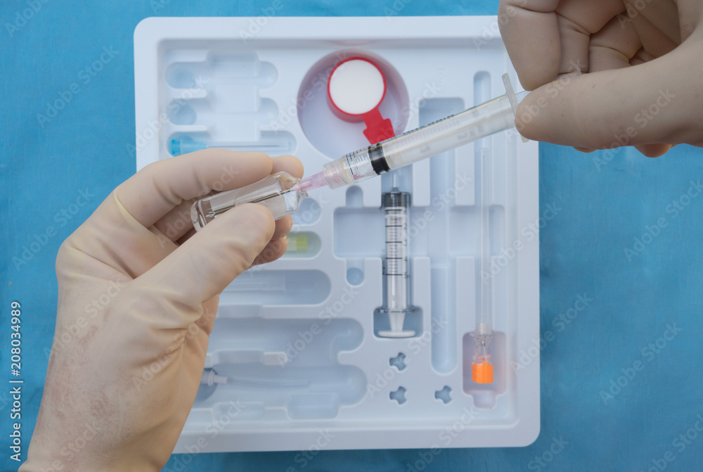 Withdrawing Novocaine from a glass vial for numbing the skin before ...