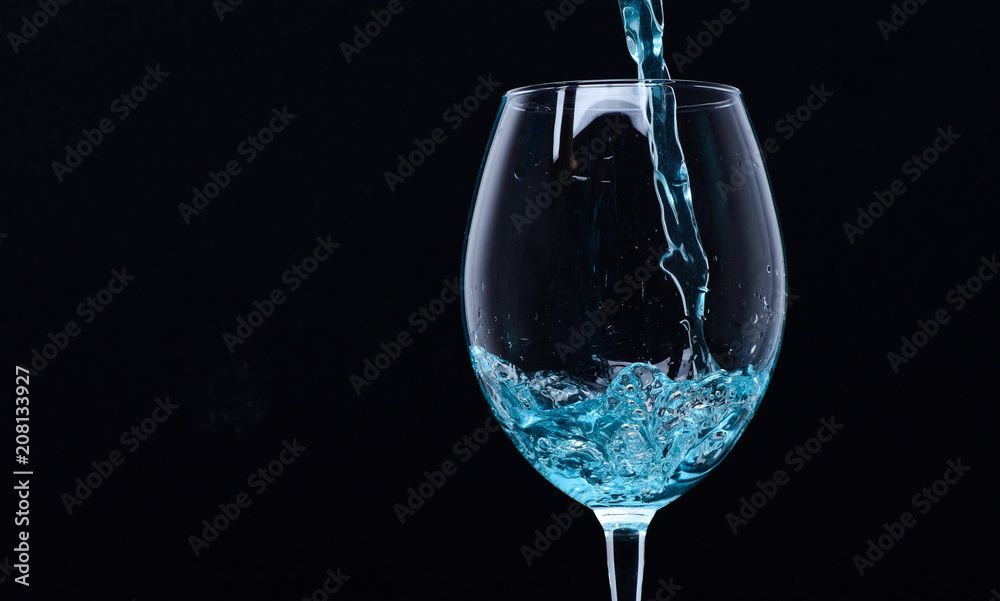 Wineglass filling with water with splashes on black background ...
