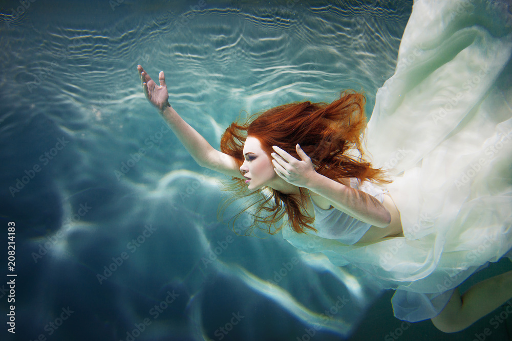 Underwater girl. Beautiful red-haired woman in a white dress, swimming ...