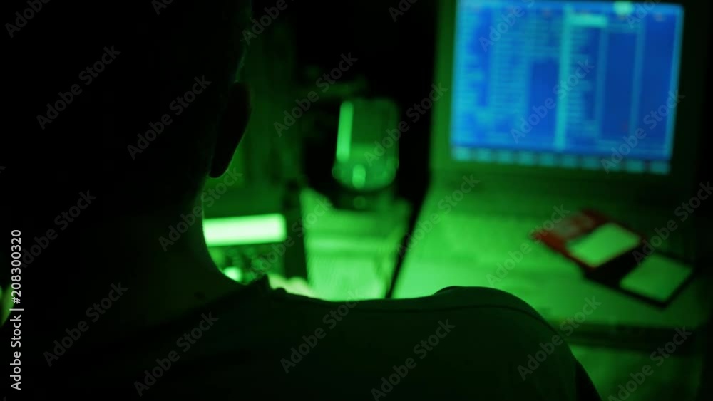 Male hacker works at dark room with green neon light with retro laptops ...