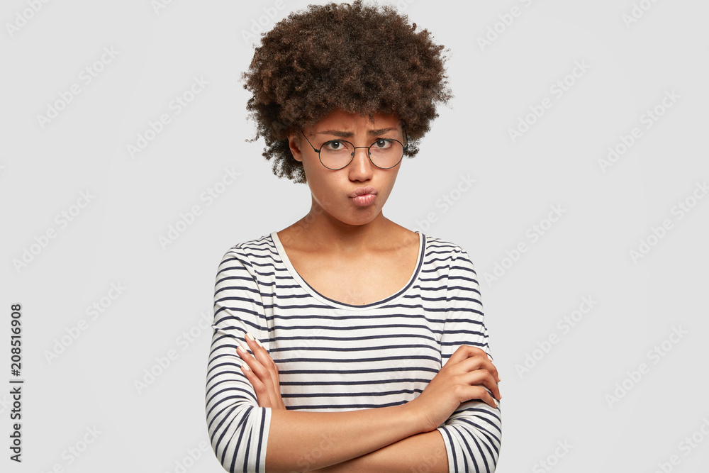 Upset sullen young female with dark skin, keeps hands crossed and looks ...
