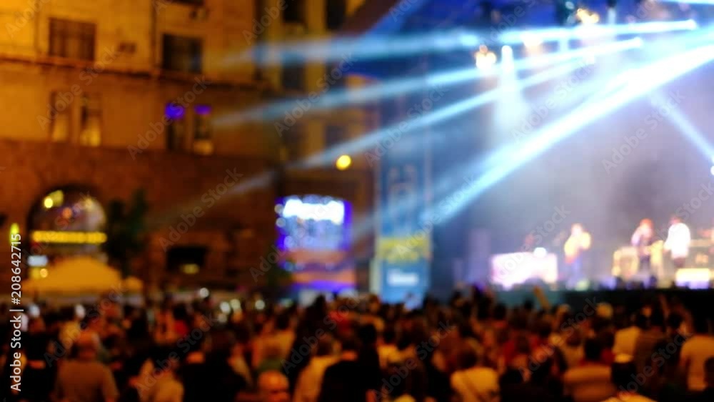 Cheering fans at a life concert. Crowd of blurred people at night stage ...