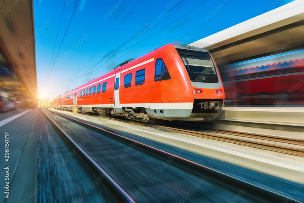 High speed red train in motion on the railway station at sunset. Modern ...