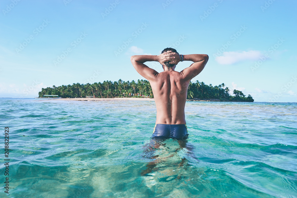 Holiday on the beach. Back view of relaxed young muscular man bathing ...
