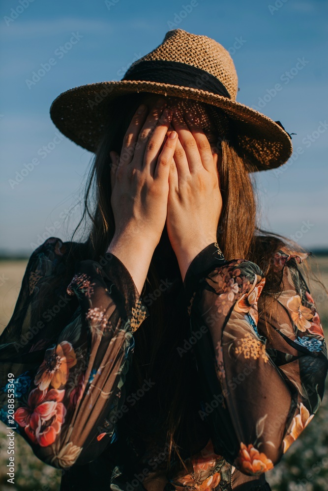 Sunny portrait of young woman hiding her face with hands and wearing ...
