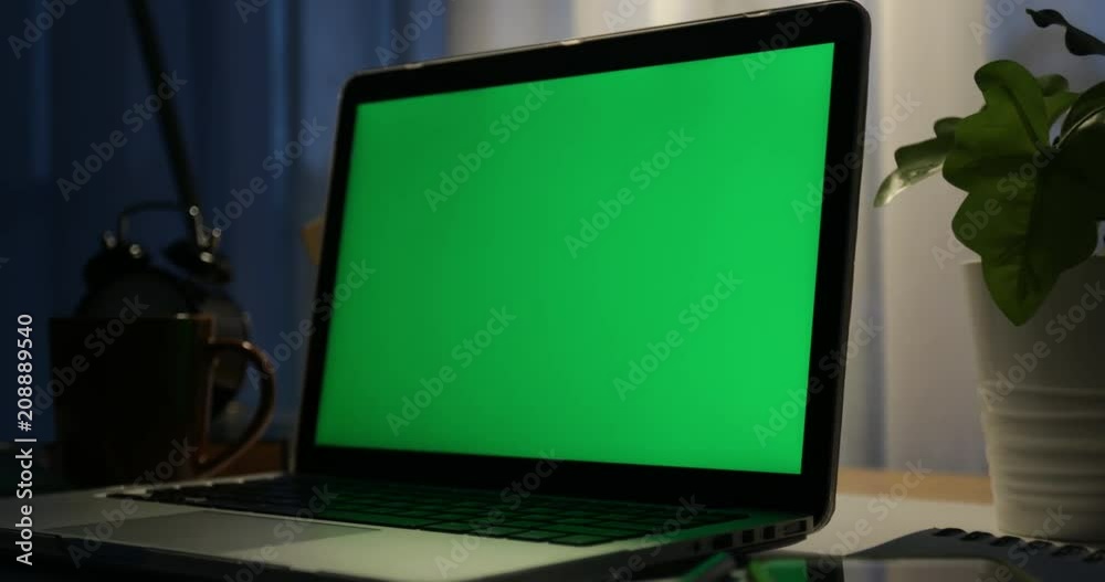 Laptop with green screen. Dark office. Dolly move right to left ...