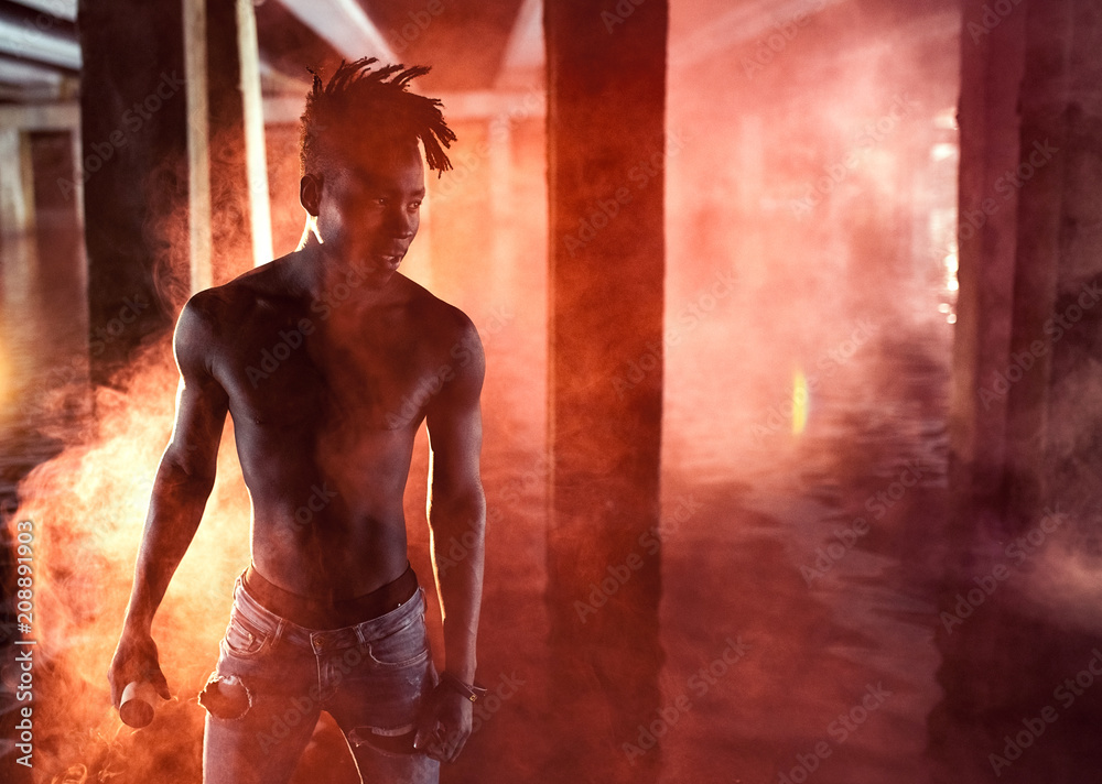 Young African man stands under bridge and holds colored red smoke bomb ...