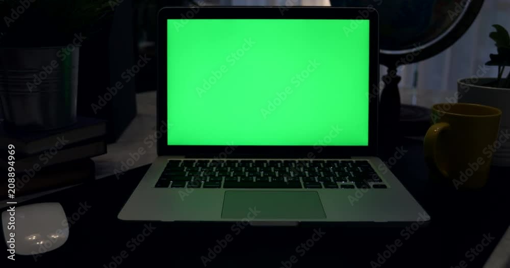 Laptop with green screen. Dark office. Dolly in . Perfect to put your ...