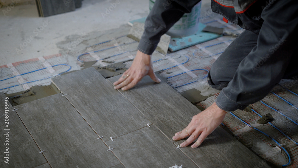 tiler is lying tile on a floor, pressing down and regulating ...