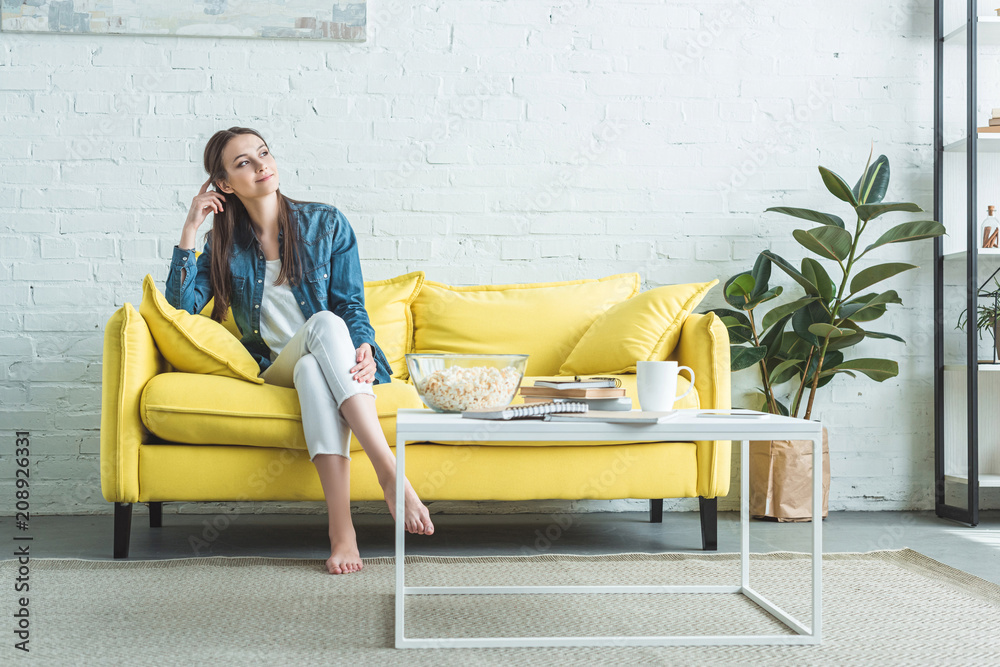 pensive smiling girl sitting on sofa and looking away at home Stock ...