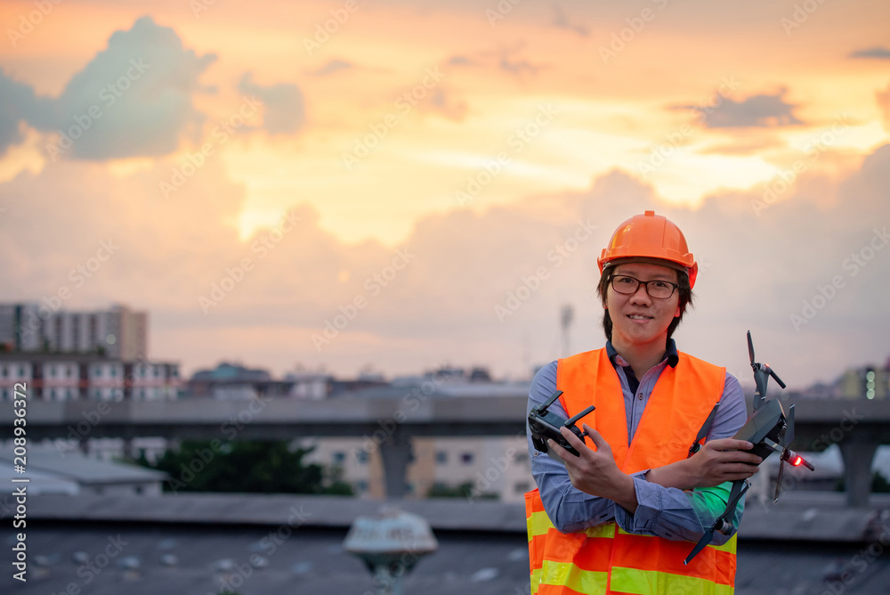 Young Asian engineer holding drone at construction site during sunset ...