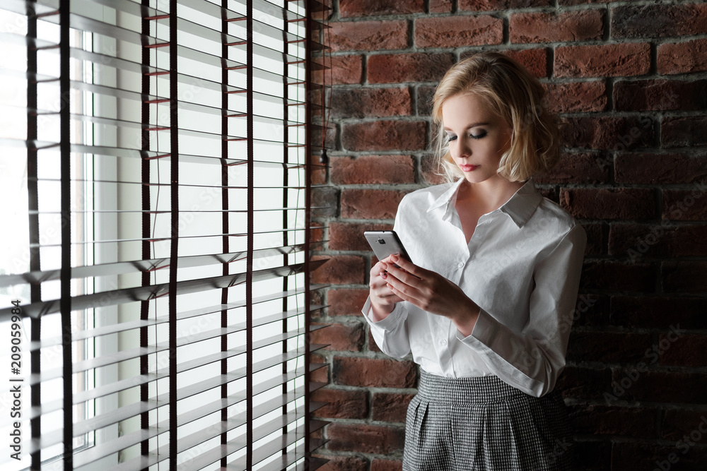 Young beautiful blonde girl stands by the window in the loft interior ...