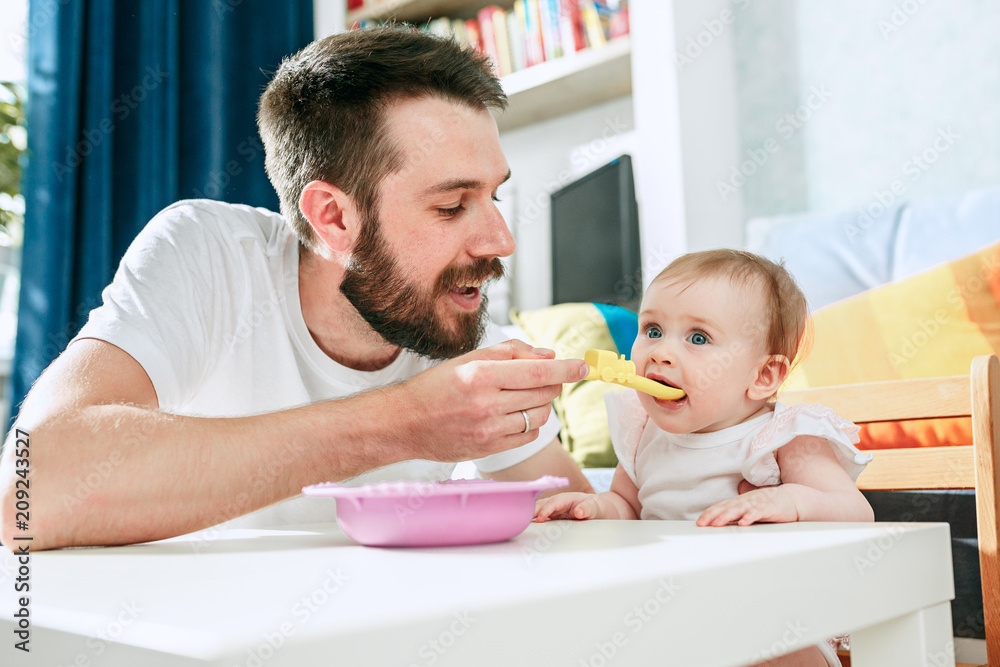 Good looking young man eating breakfast and feeding her baby girl at ...