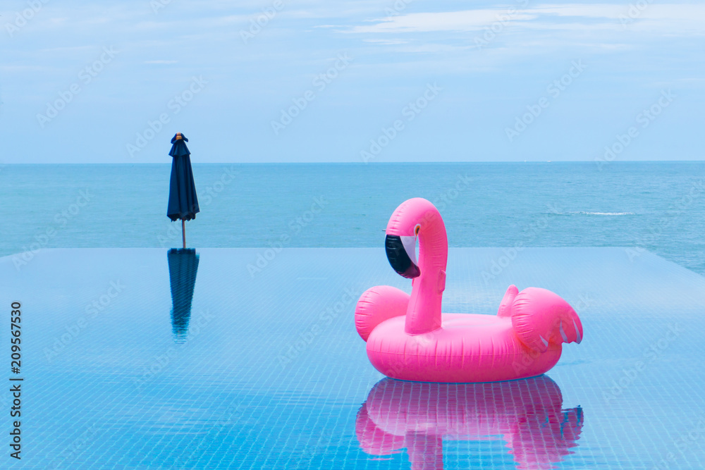 flamingo raft floating in swimming pool in front of the sea and island ...