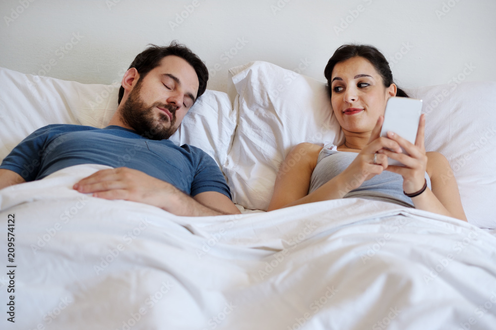 Cheating Wife Using Mobile Phone Lying In Bed Next To His Sleeping