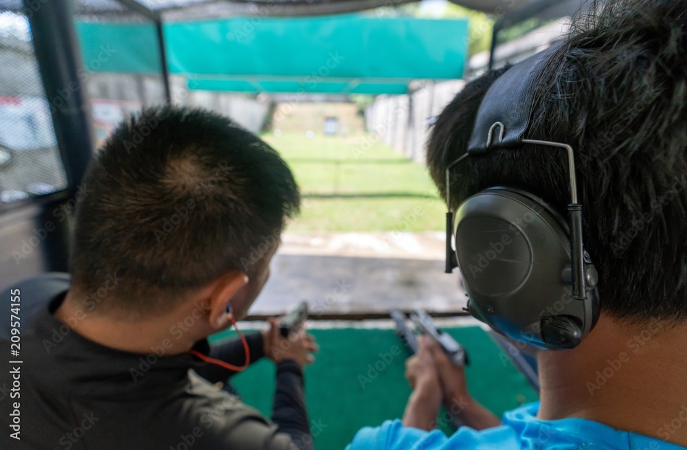 Rear view of a Two Man Shooting with Gun at Target in Shooting Range ...