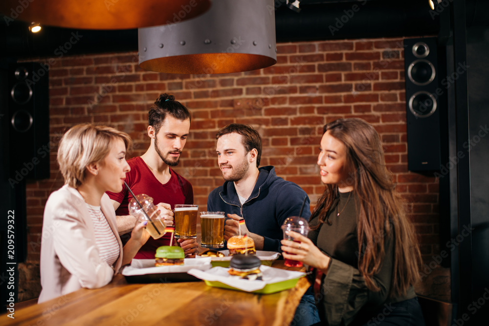 Group of joyful young students tasting fast food cheeseburgers with ...