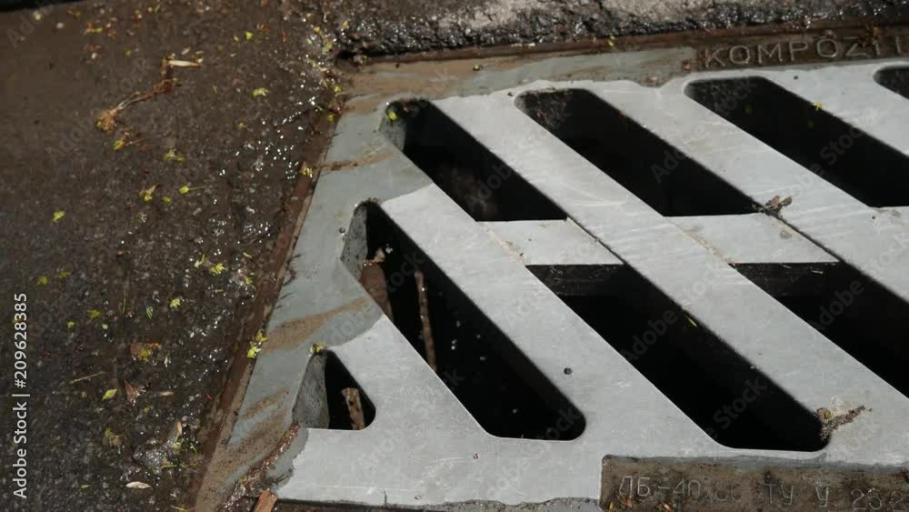 Rain water flowing into a drain.Rainwater flows on the asphalt road and ...