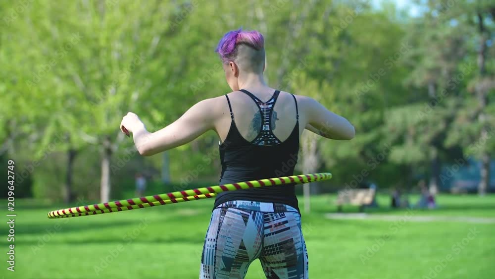 Medium slow motion rear view of a beautiful young woman rotating a hula ...