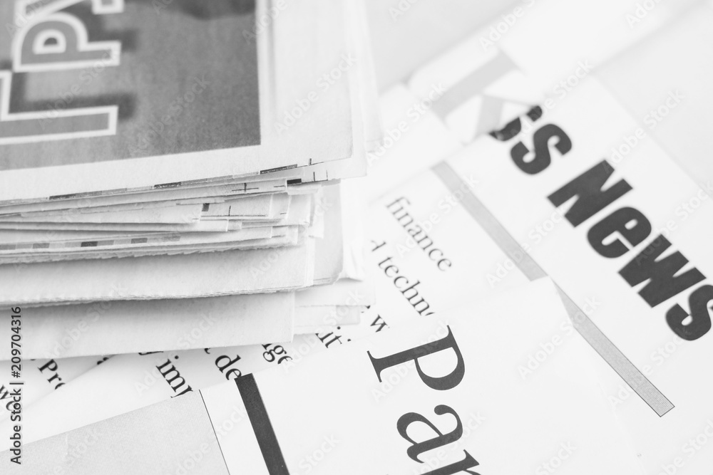 Pile of newspapers and scattered news pages on table. Headlines and ...