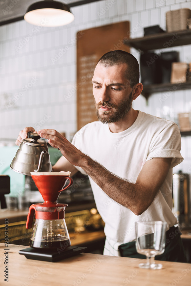 Young barista standing at bar counter and thoughtfully preparing pour ...