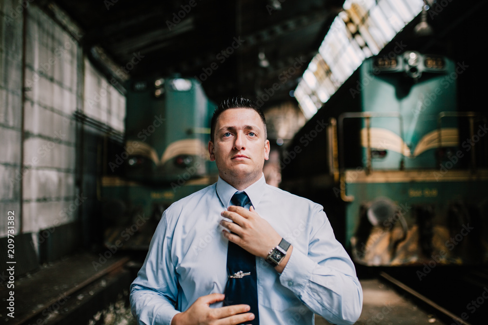 Young railroad engineer tie a tie in old locomotive depot with two ...