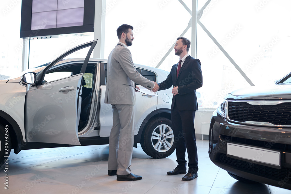 Full length side view of handsome car salesman shaking hands with ...