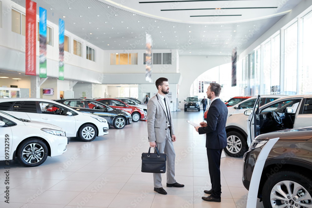 Full length portrait of handsome car salesman talking to customer in ...