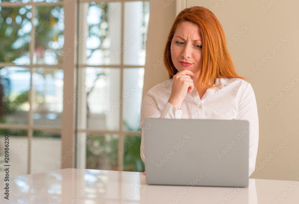 Redhead woman using computer laptop at home serious face thinking about ...