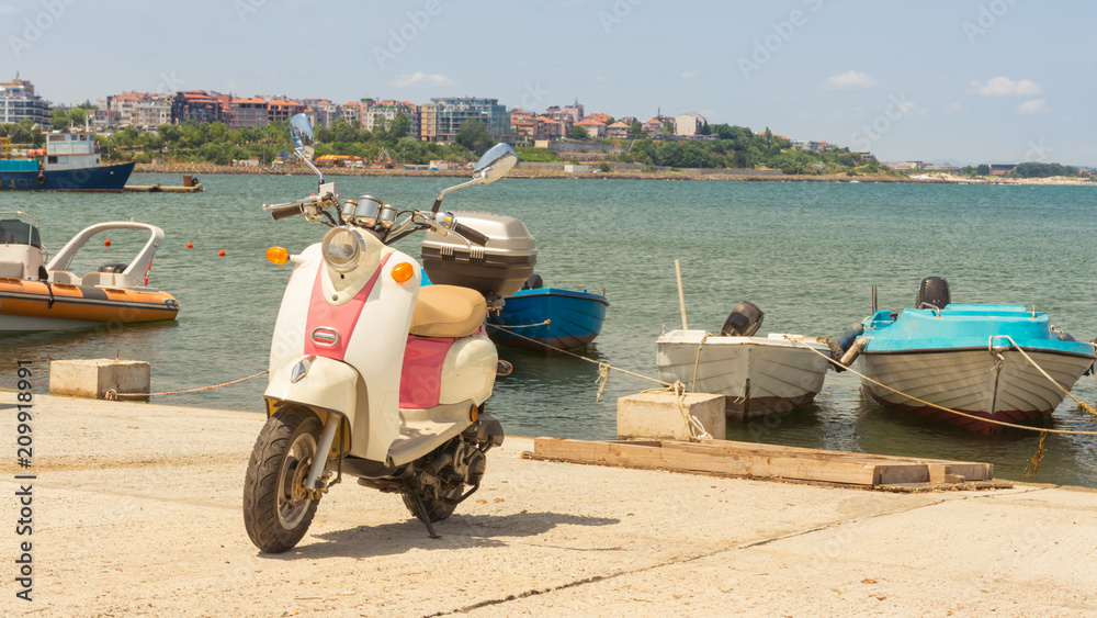 Scooter parked on a coastal street near fishing boats at summer Stock ...