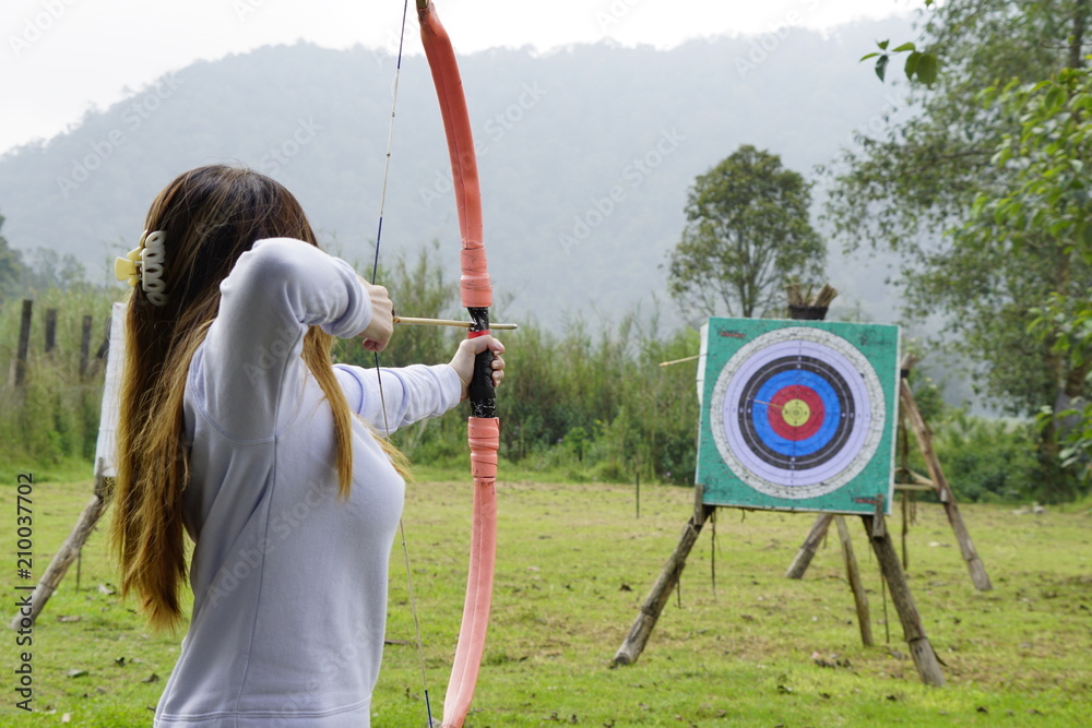 Young woman is aiming in archery practice n the field with a target in ...