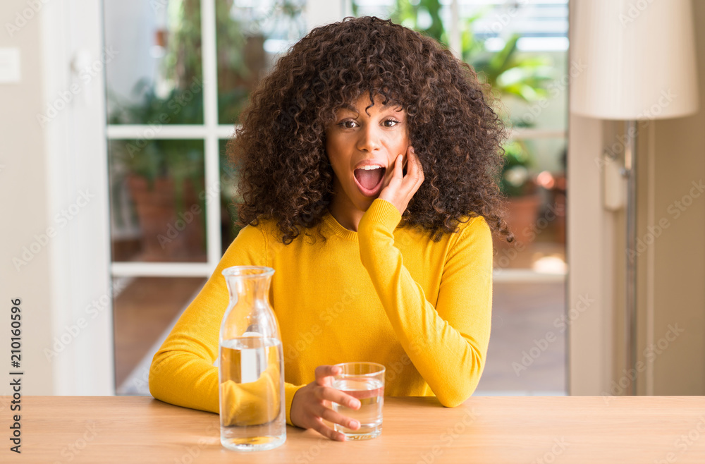 African american woman drinking a glass of water at home scared in ...