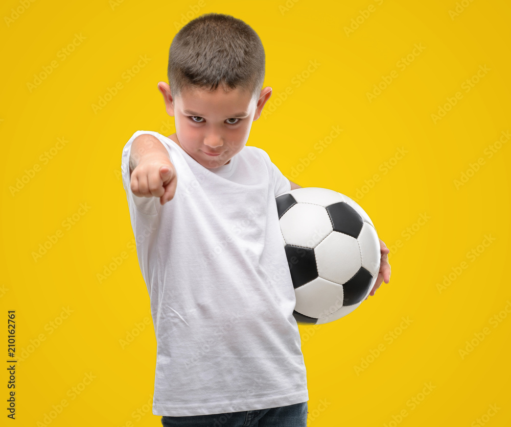 Dark haired little child playing with soccer ball pointing with finger ...