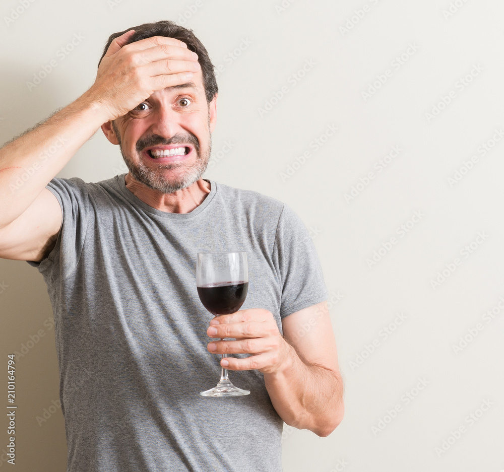 Senior man drinking red wine in a glass stressed with hand on head ...