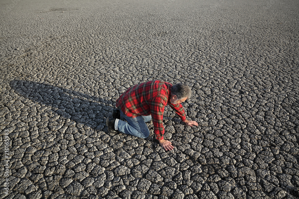 Desperate man kneeling and praying at dry cracked land after drought ...