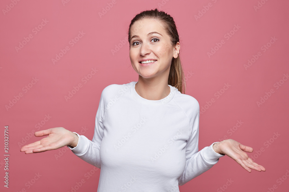Hesitant beautiful pleased young Caucasian female shrugs shoulders, can ...