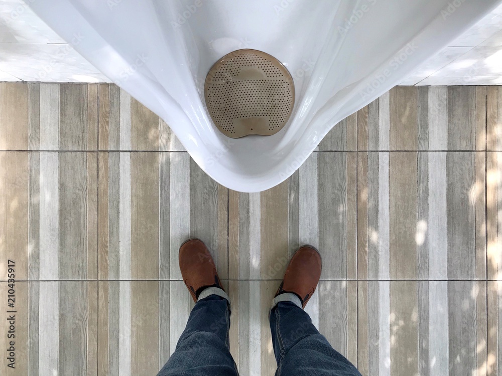 Man standing in front of urinal Top view of a man legs in front of ...