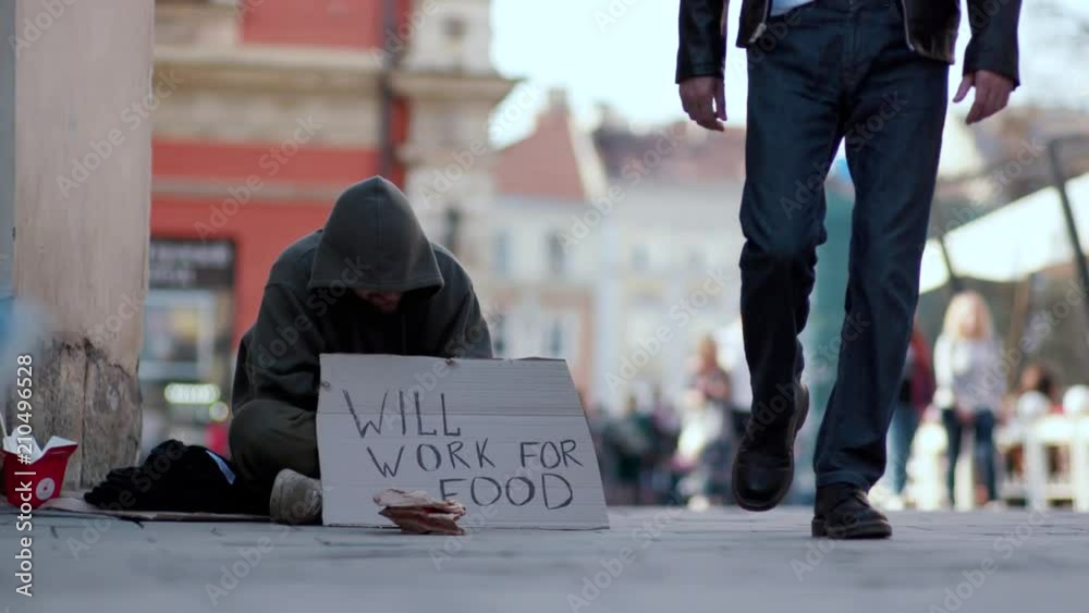 Stockvideo Homeless man sitting on a street with sign people walk ...