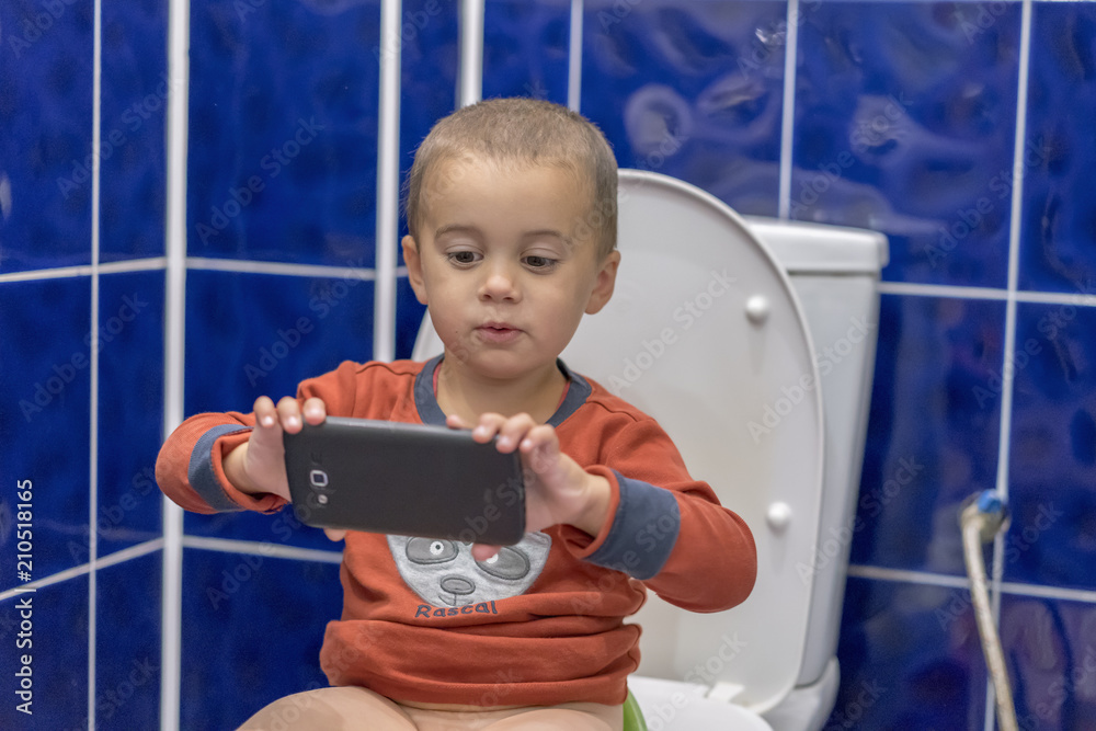 Cute toddler boy with smartphone in the bathroom. Little boy sitting on ...