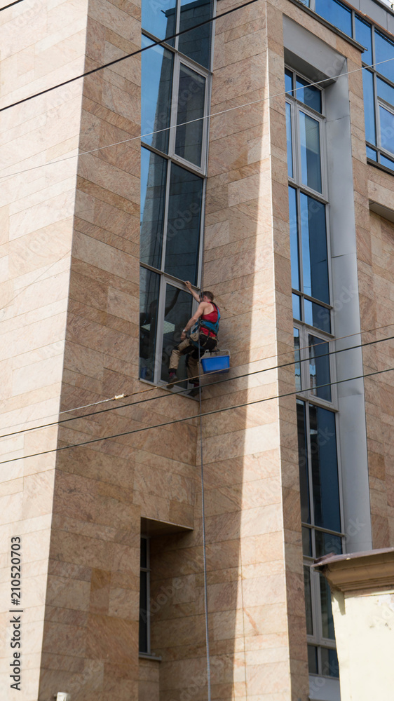 A worker is hanging on ropes and doing works for cleaning and washing ...