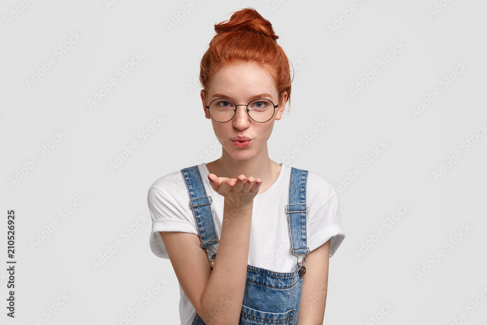 Indoor shot of pretty young red haired female has freckled face, blows ...