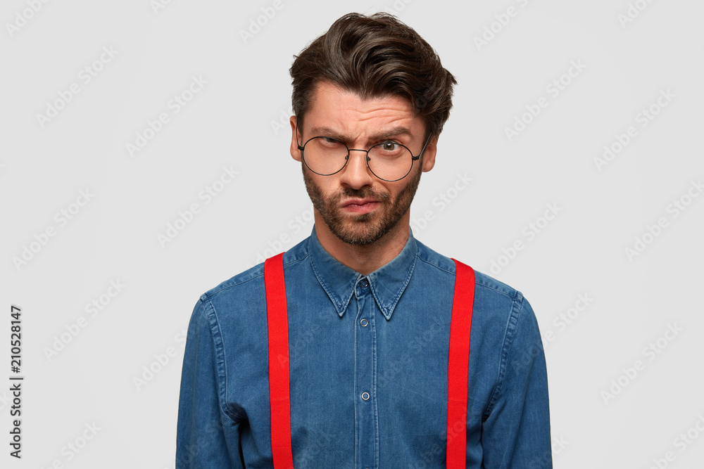 Serious grumpy male with stubble, looks with annoyed disturbed ...